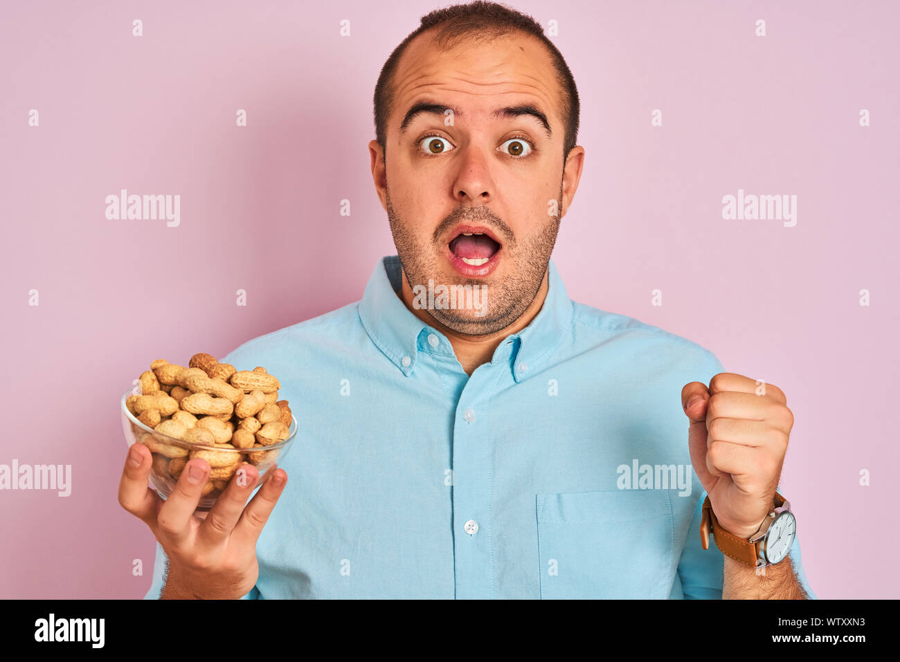 Young man holding bowl with peanuts standing over isolated pink ...
