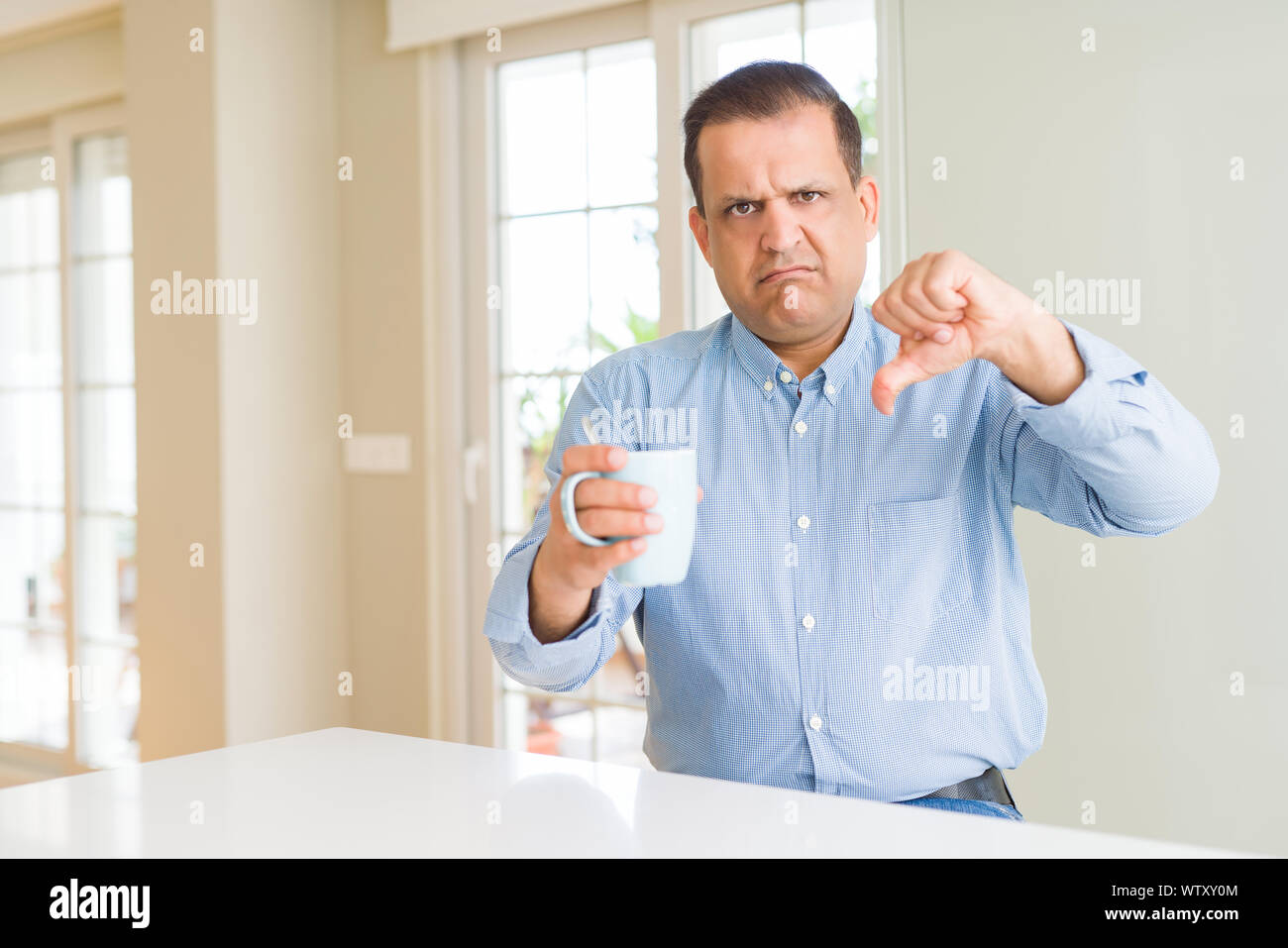 Middle age man drinking coffee in the morning at home with angry face ...