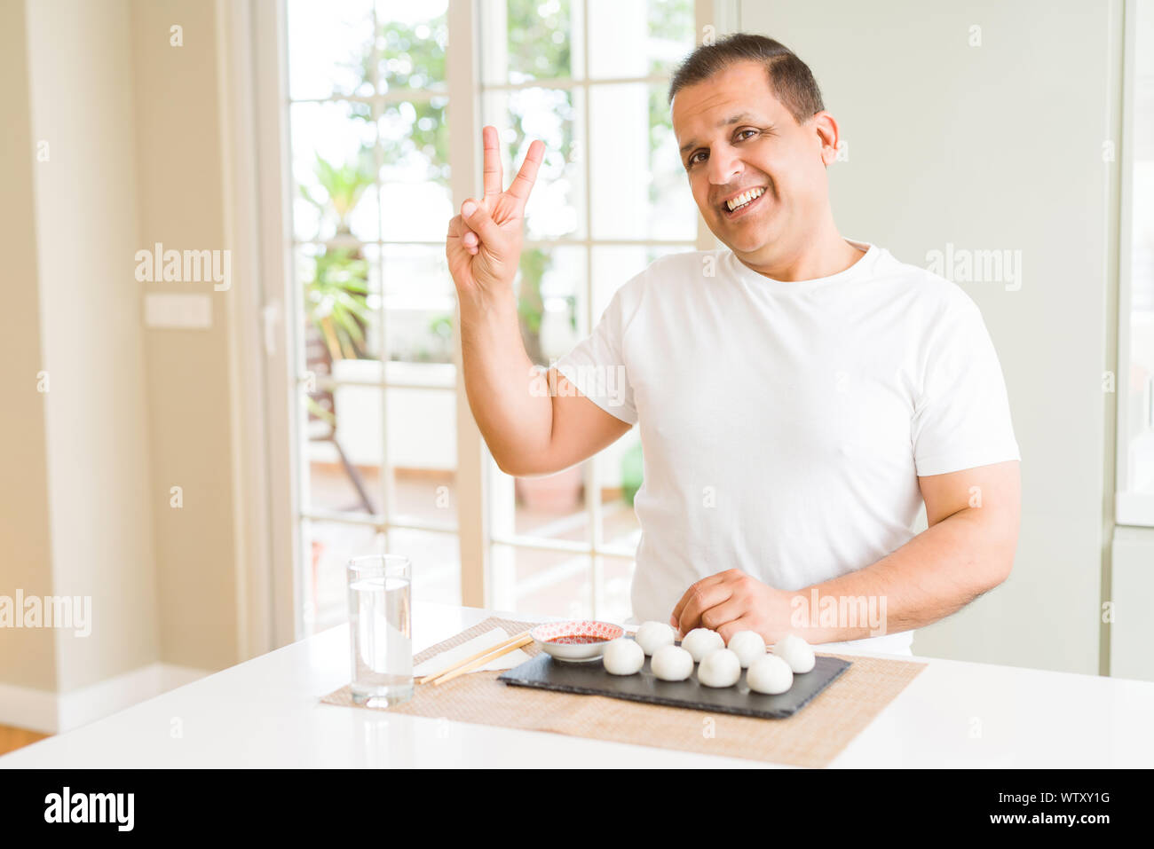 Middle age man eating asian dumplings at home smiling with happy face ...