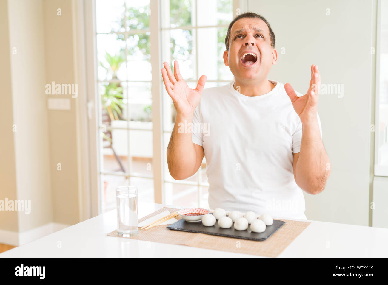 Middle age man eating asian dumplings at home celebrating mad and crazy ...