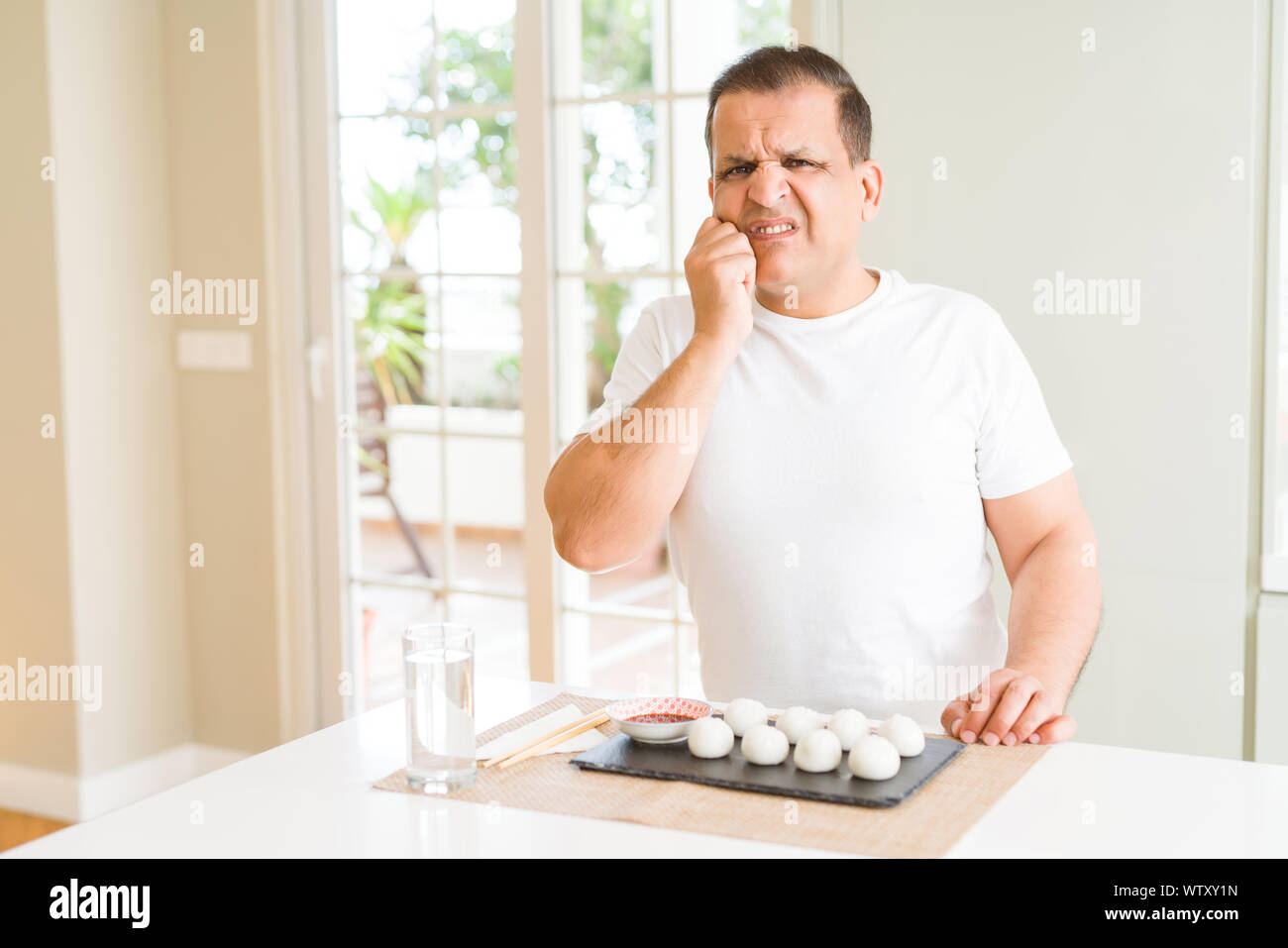 Middle age man eating asian dumplings at home looking stressed and ...