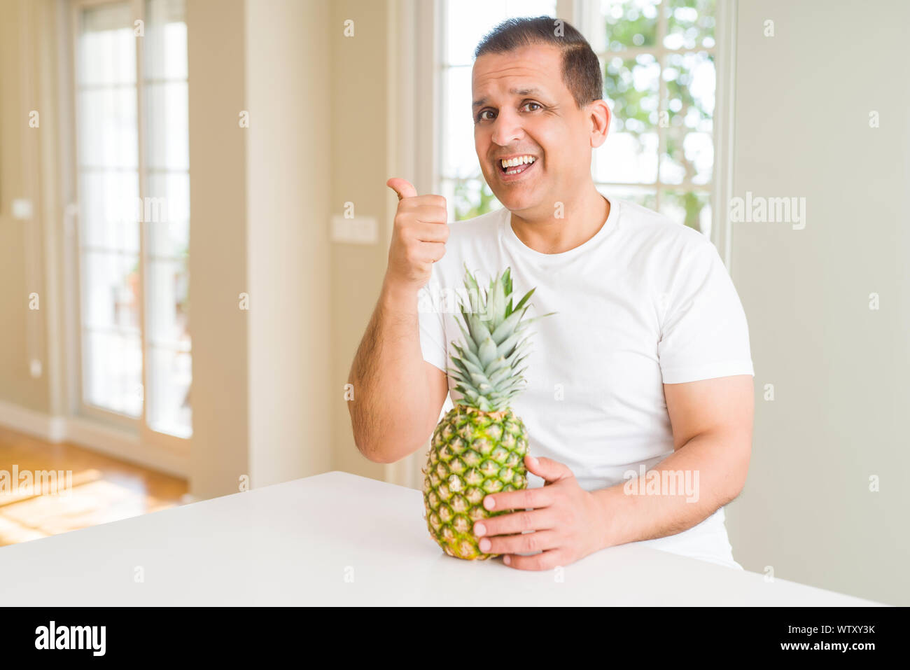 Middle age man eating fresh tropical pineapple at home pointing and ...