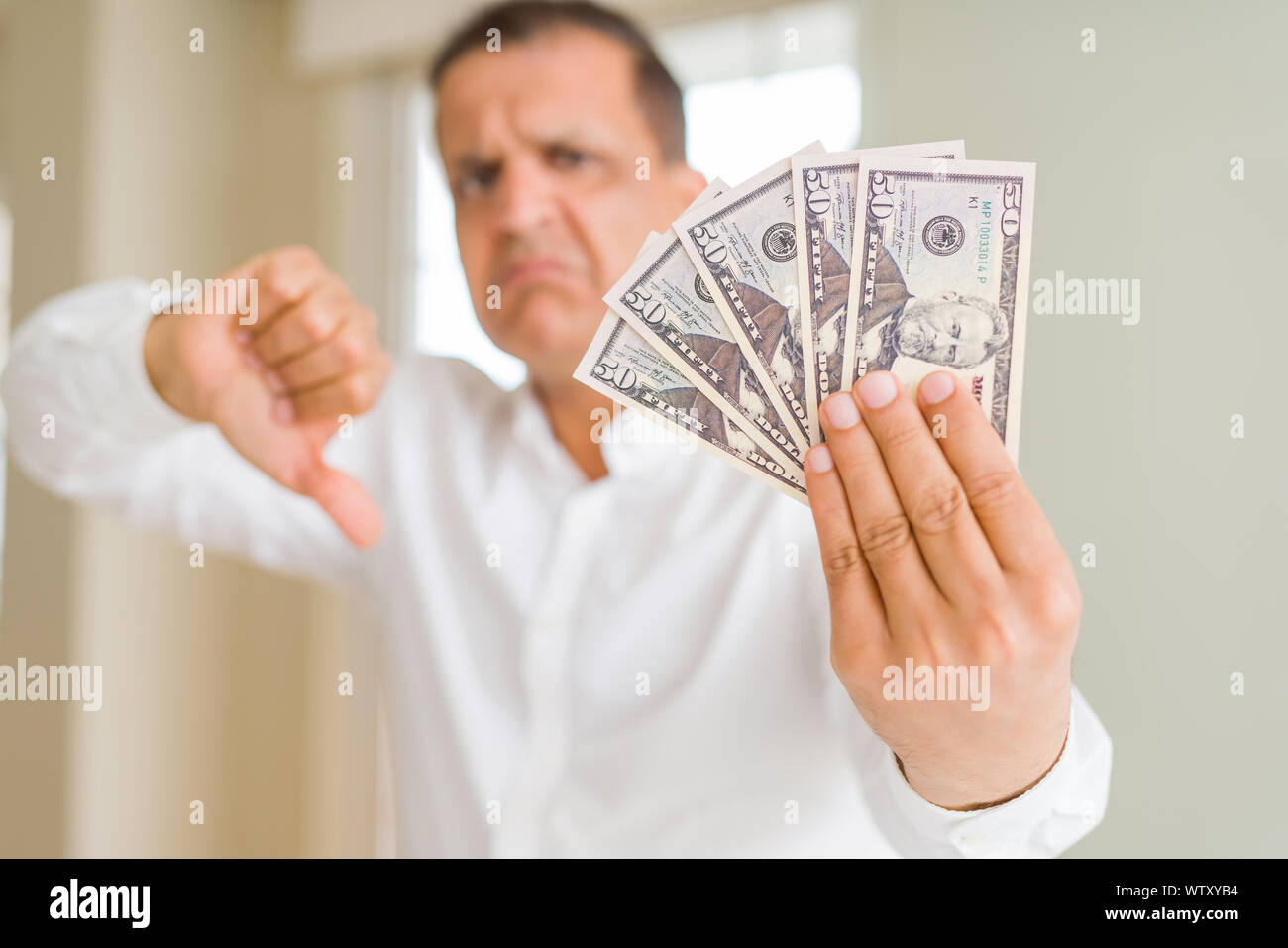 Middle age man holding bunch of dollars with angry face, negative sign ...