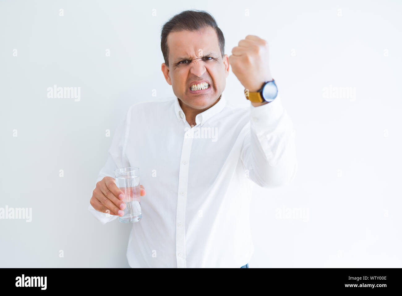 Middle age man drinking a glass of water over white background annoyed ...