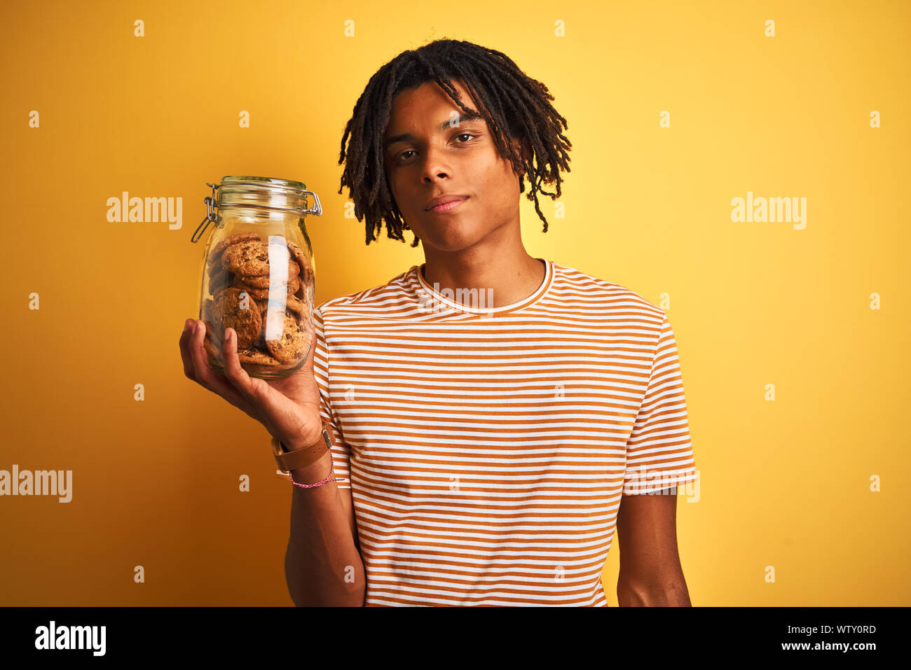 Afro american man with dreadlocks holding jar of cookies over isolated ...