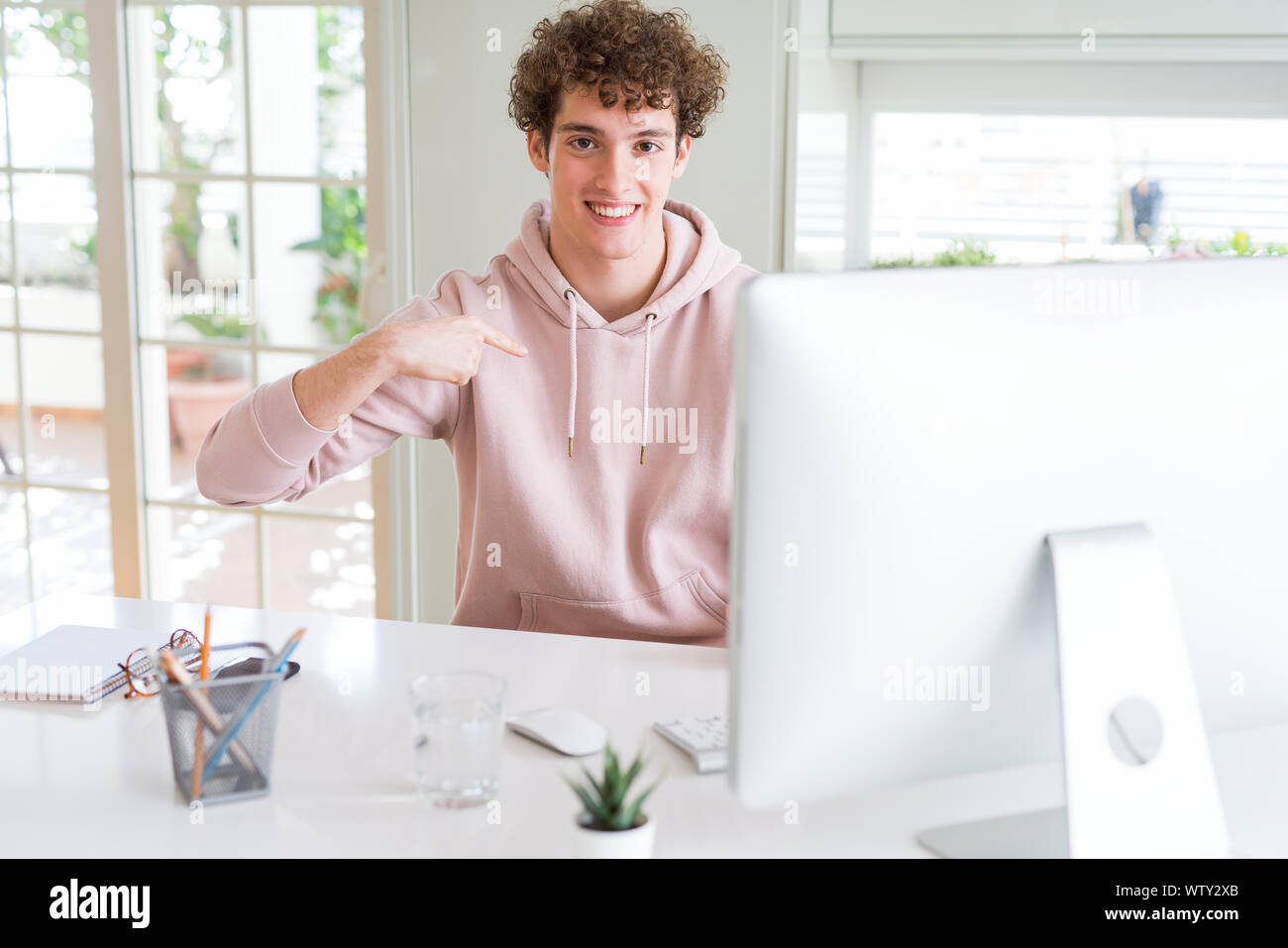 Young student man using computer with surprise face pointing finger to ...