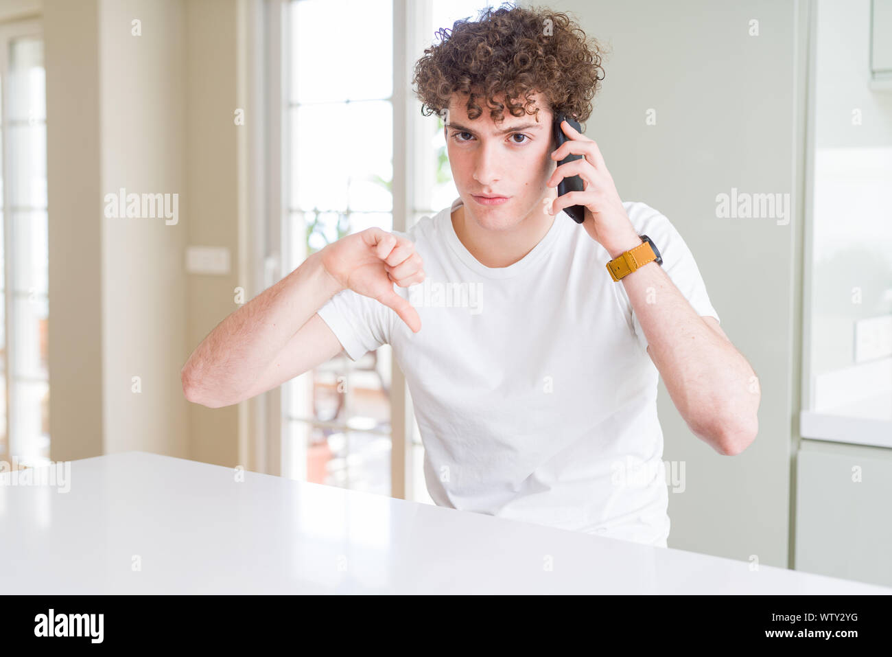 Young man talking on the phone at home with angry face, negative sign ...