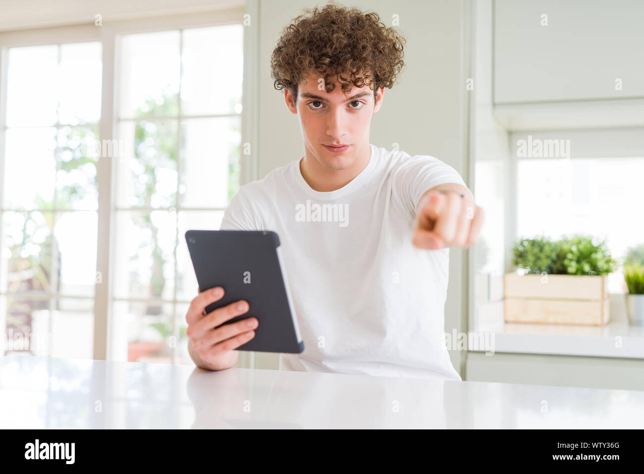 Young man using touchpad tablet pointing with finger to the camera and ...