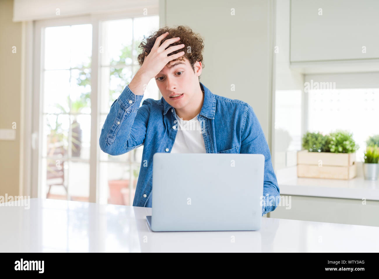 Young man using computer laptop stressed with hand on head, shocked ...