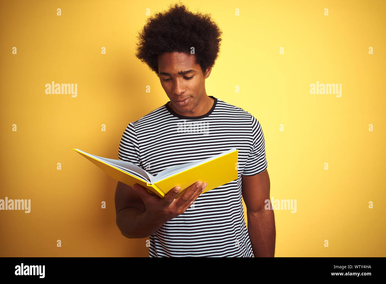 Afro american student man reading book standing over isolated yellow ...