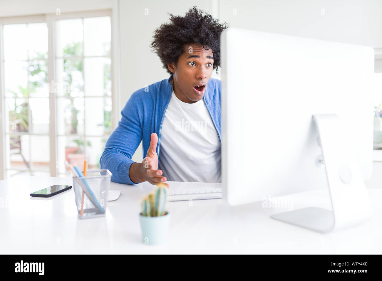 African American man working using computer scared in shock with a ...