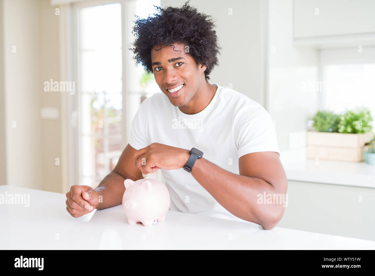 African American man putting a coin inside piggy bank with a happy face ...