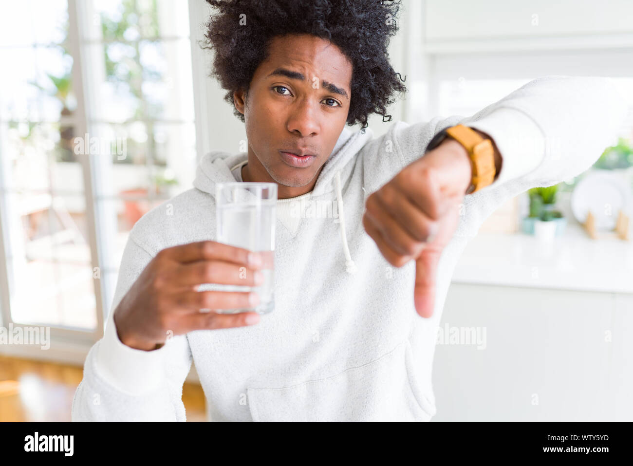 African American man drinking a glass of water at home with angry face ...