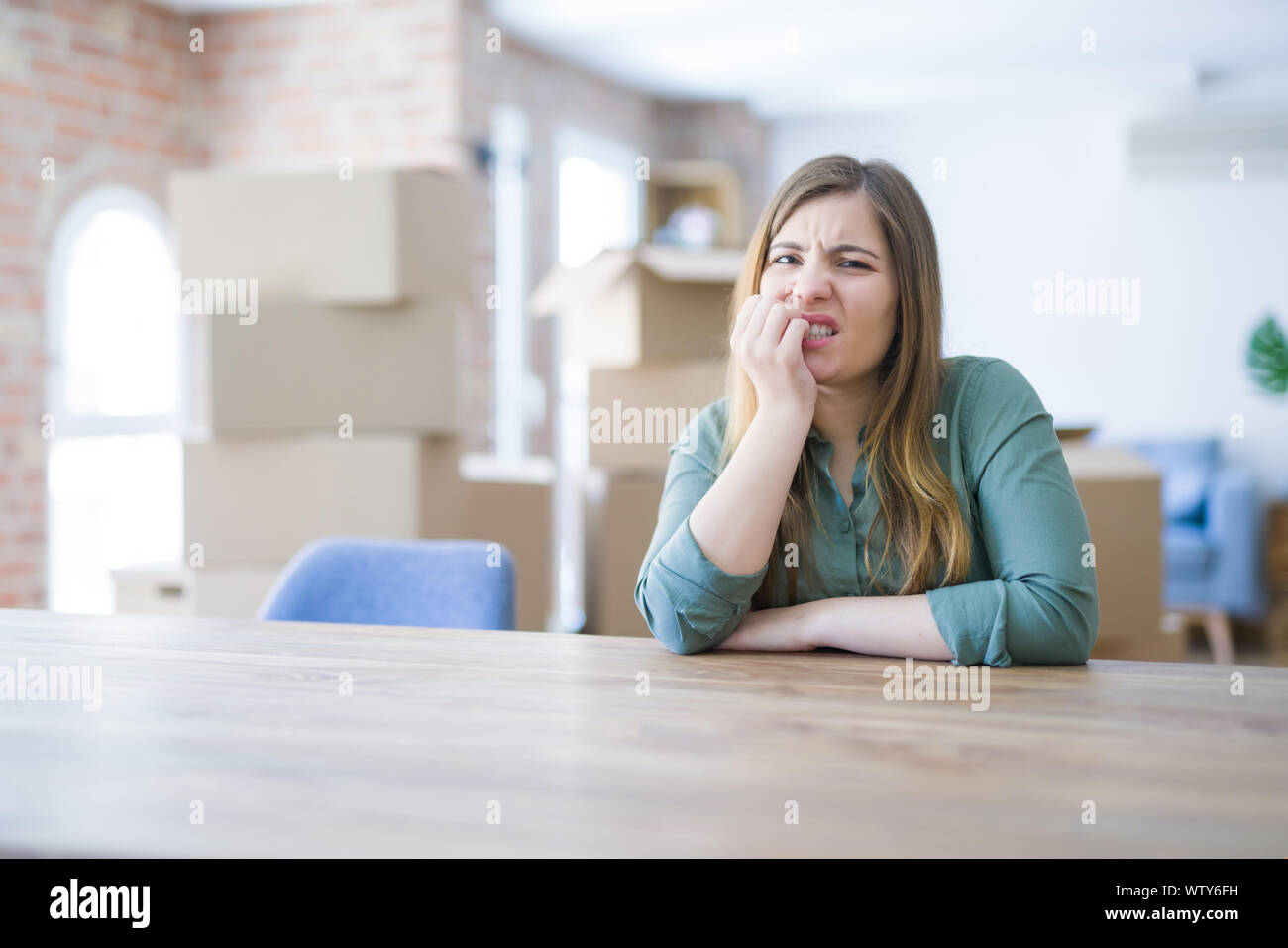 Young woman sitting on the table with cardboard boxes behind her moving ...