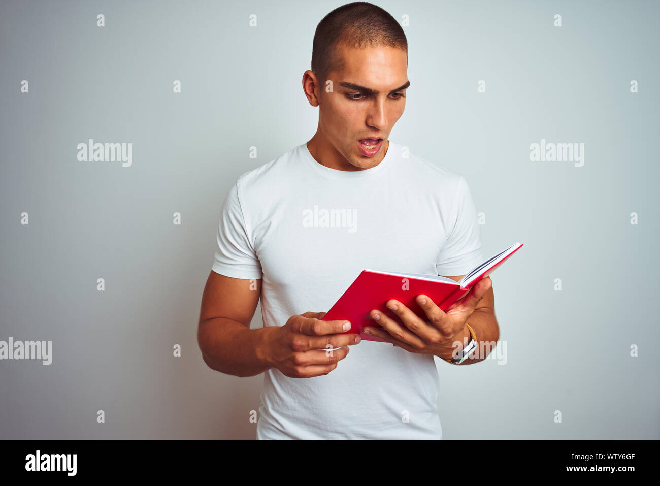 Young handsome man reading red book over white isolated background ...
