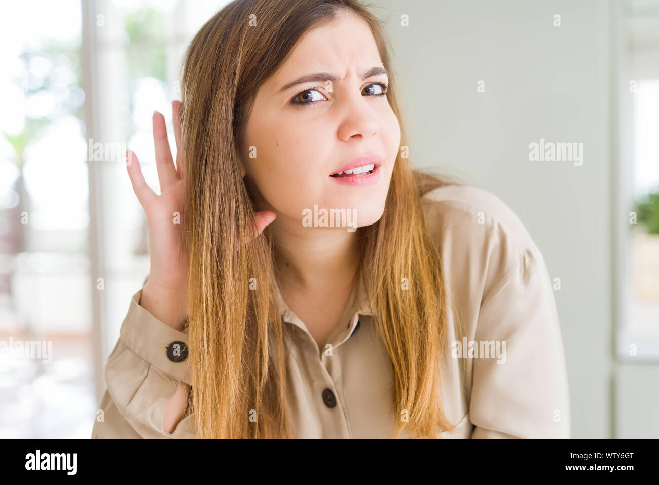 Beautiful young woman at home smiling with hand over ear listening an ...
