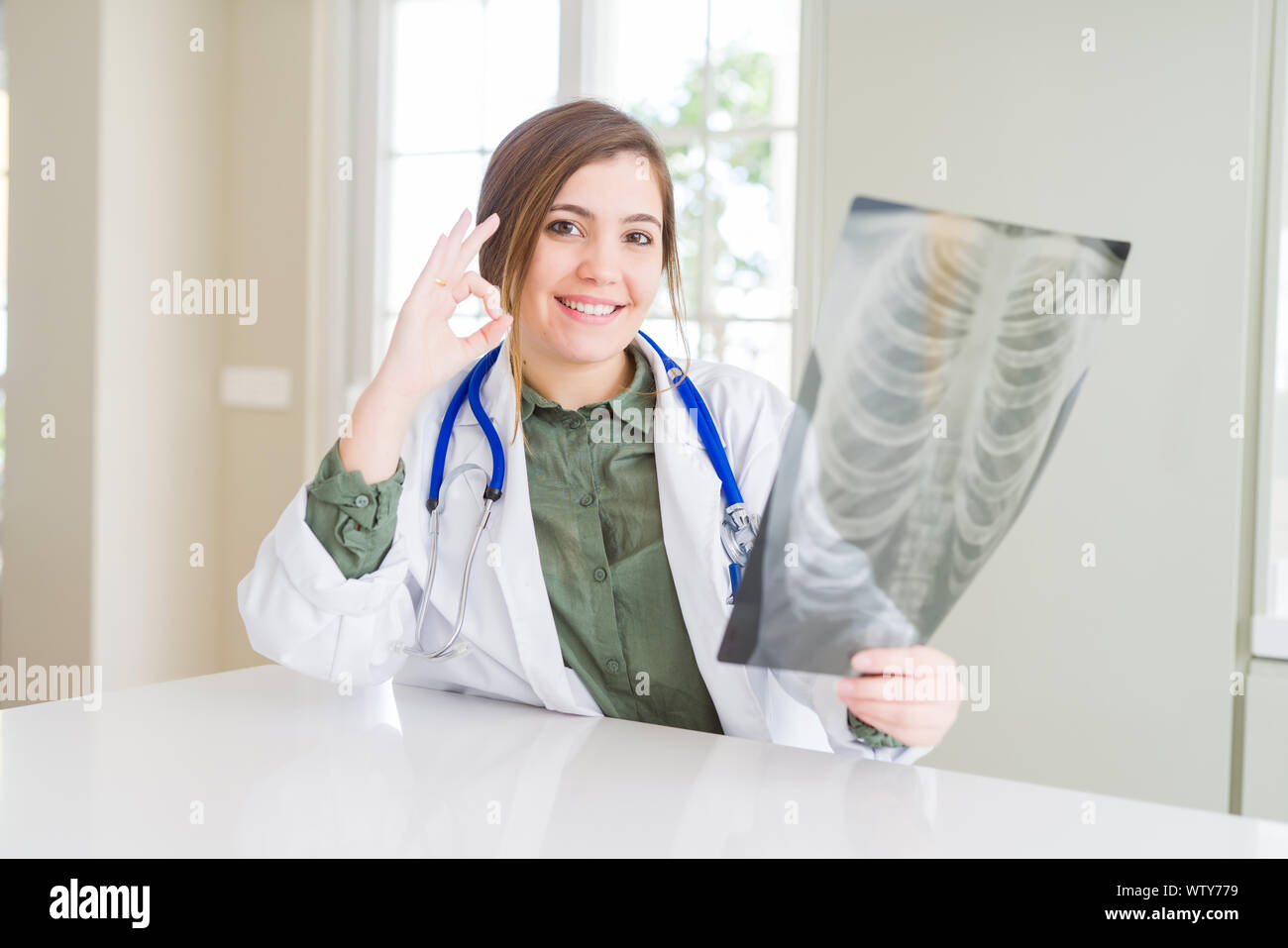 Beautiful young doctor woman looking at chest radiography doing ok sign ...