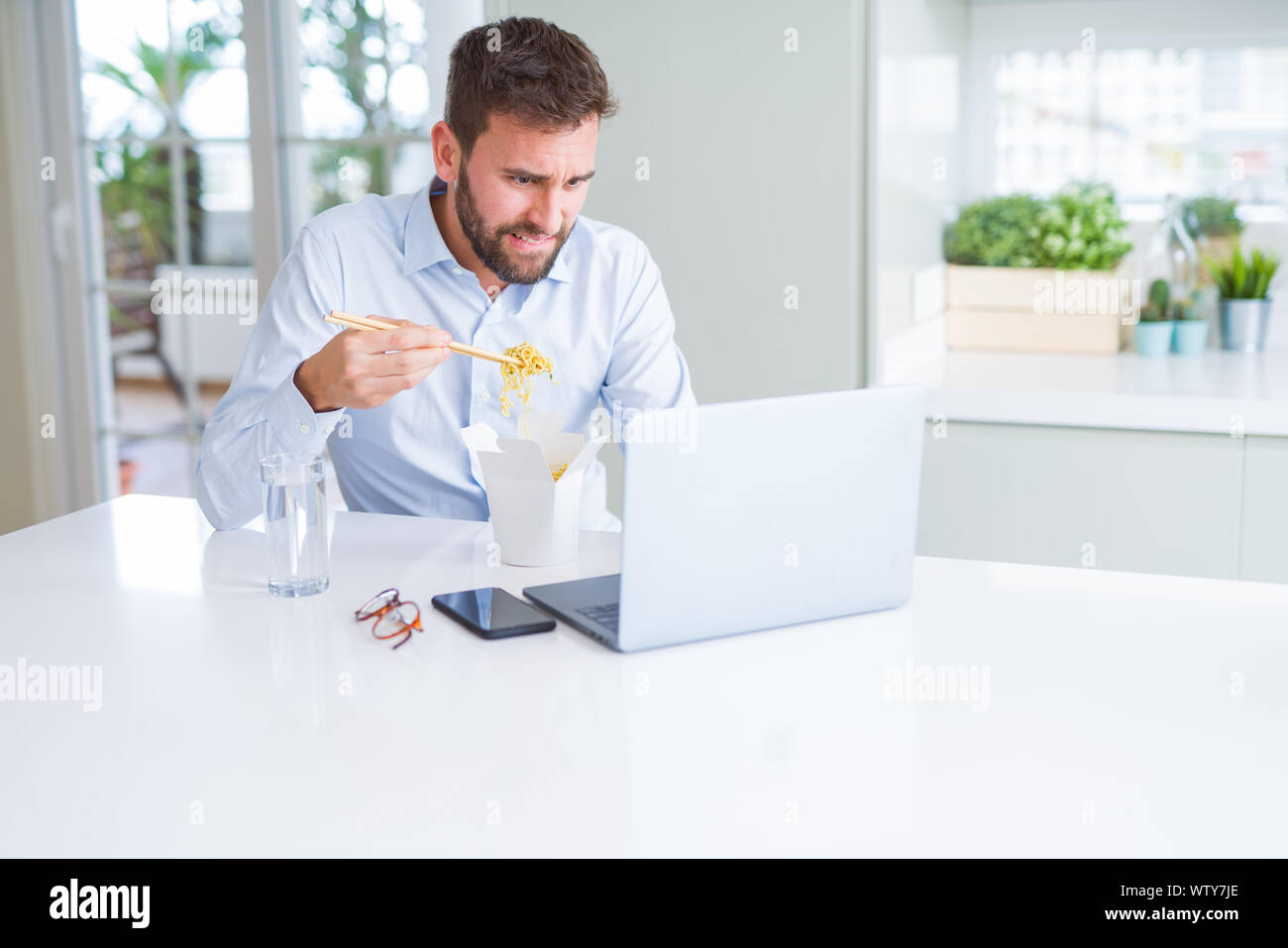 Business man eating take away asian noodles food while working using ...