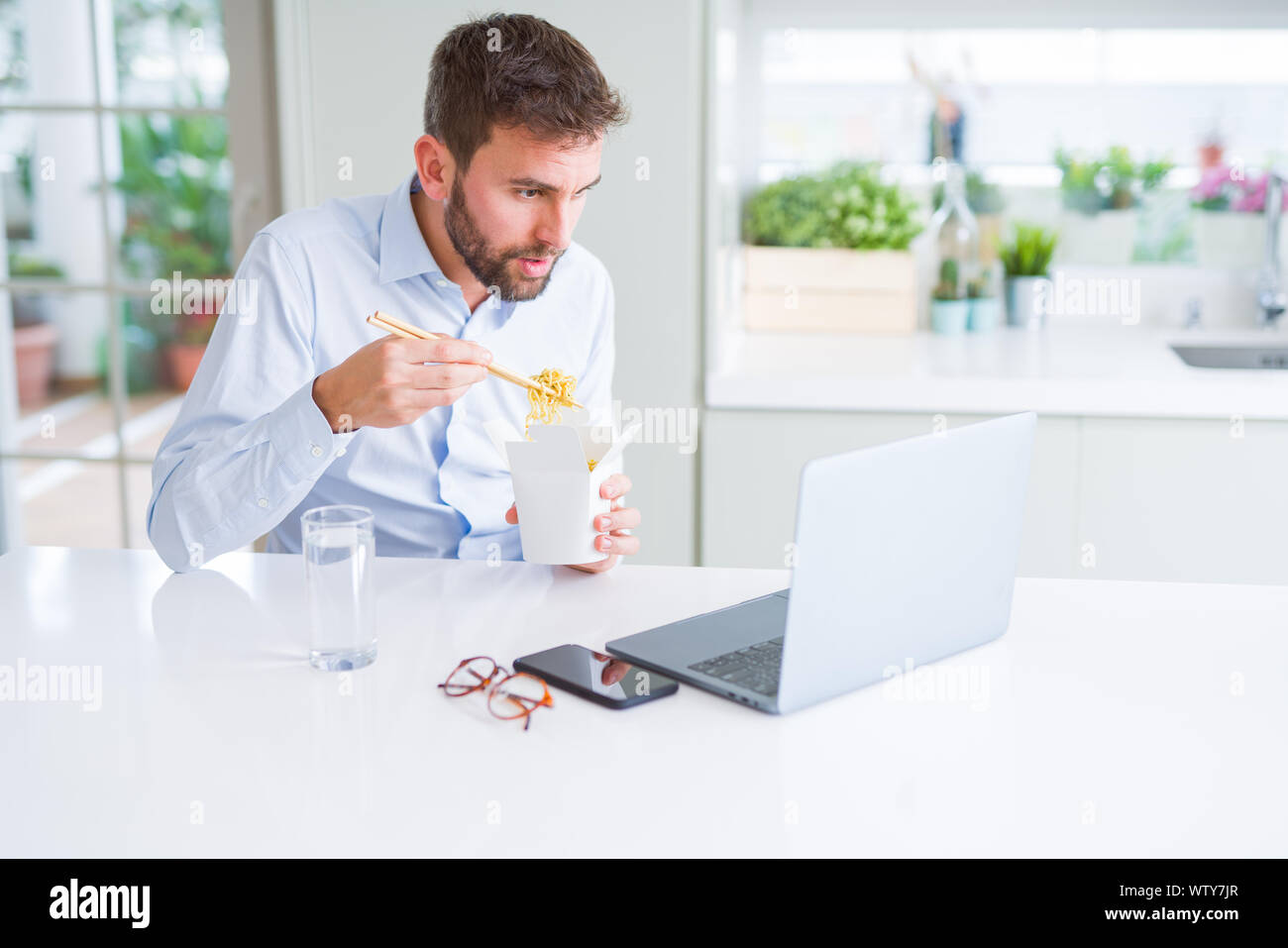 Business man eating take away asian noodles food while working using ...
