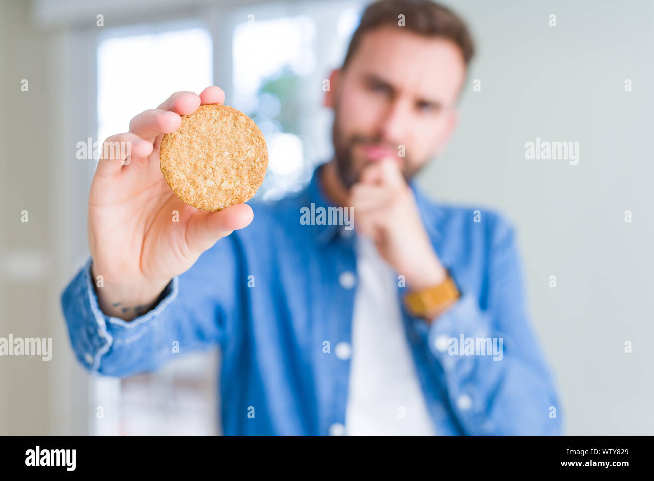 Handsome man eating healthy whole grain biscuit serious face thinking ...