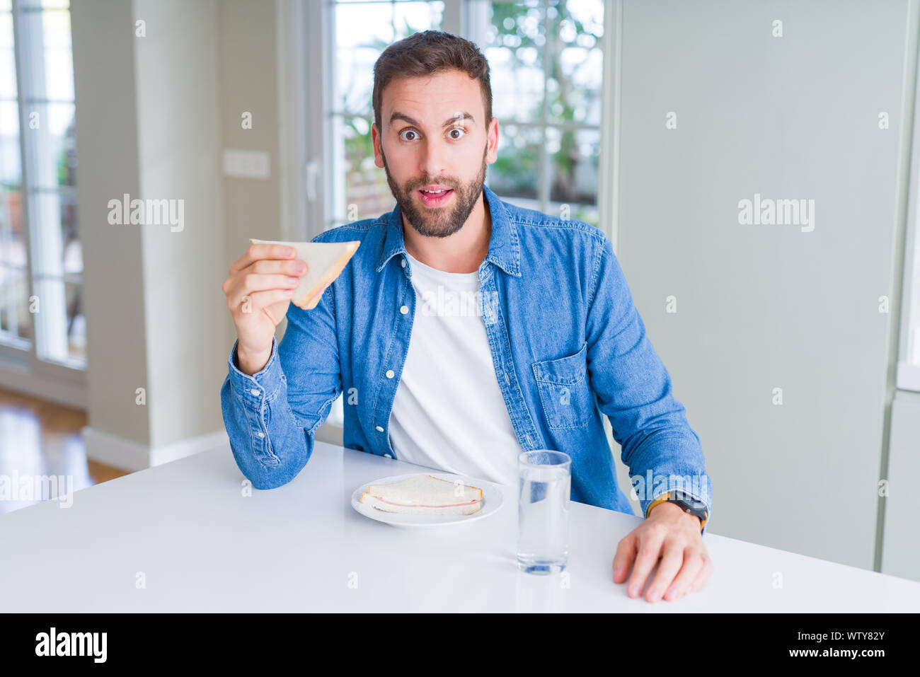 Handsome man eating healthy sandwich scared in shock with a surprise ...