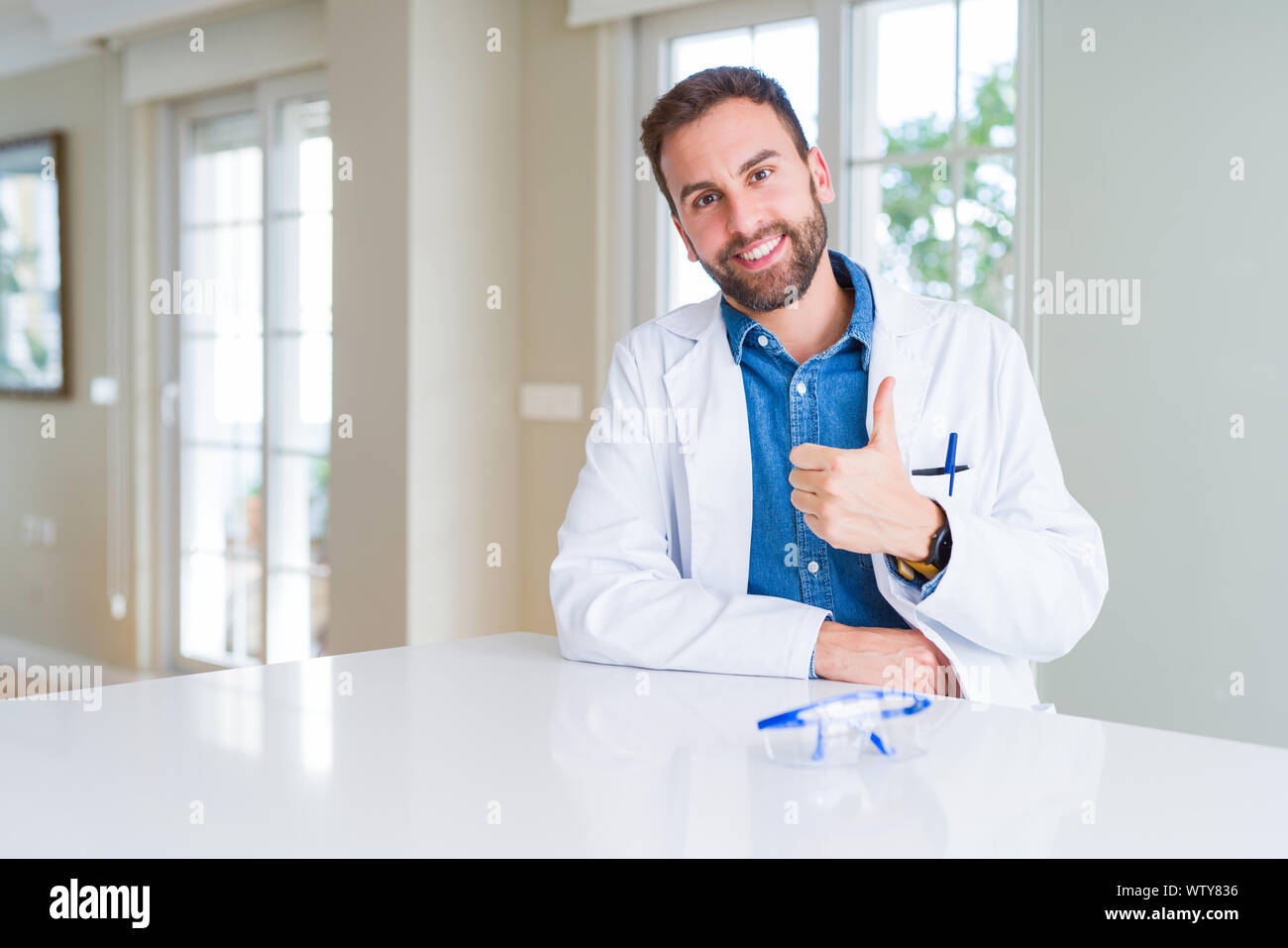Handsome scientist man wearing white robe and safety glasses doing ...