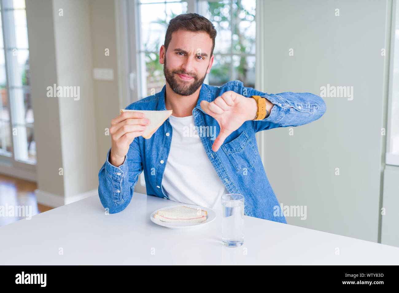 Handsome man eating healthy sandwich with angry face, negative sign ...