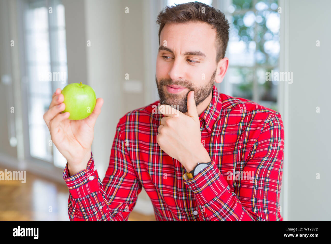 Handsome man eating fresh healthy green apple serious face thinking ...