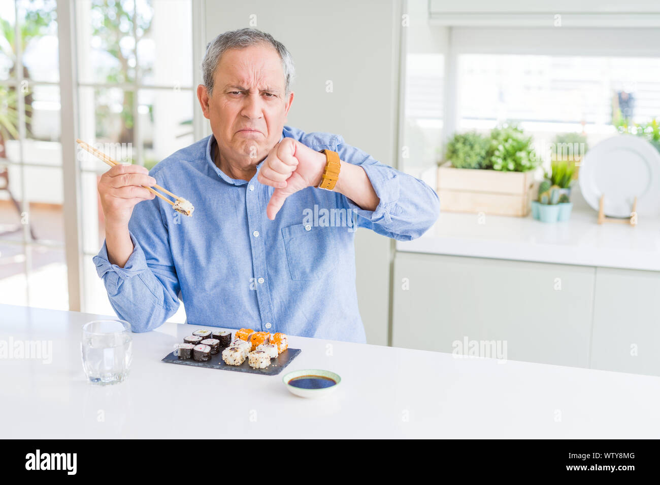 Handsome senior man eating take away sushi using chopsticks at home ...