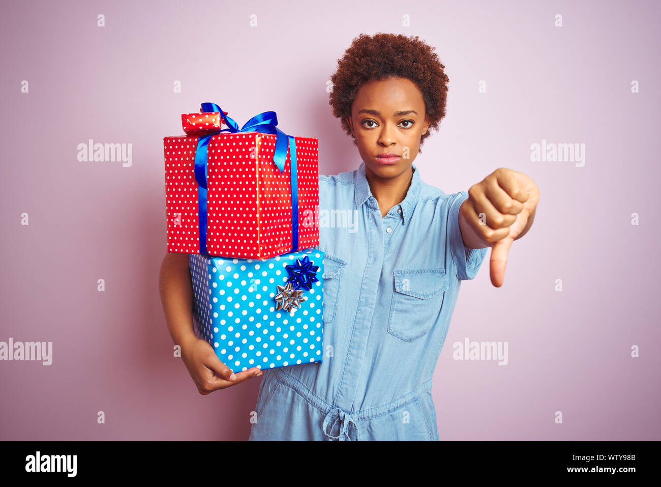 African american woman holding birthday gifts over pink isolated ...