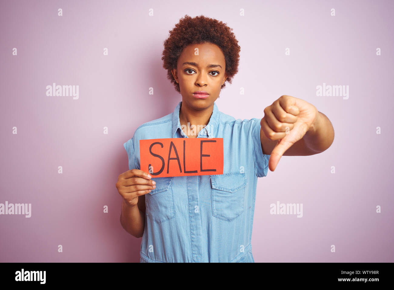 African american woman holding sale board over pink isolated background ...