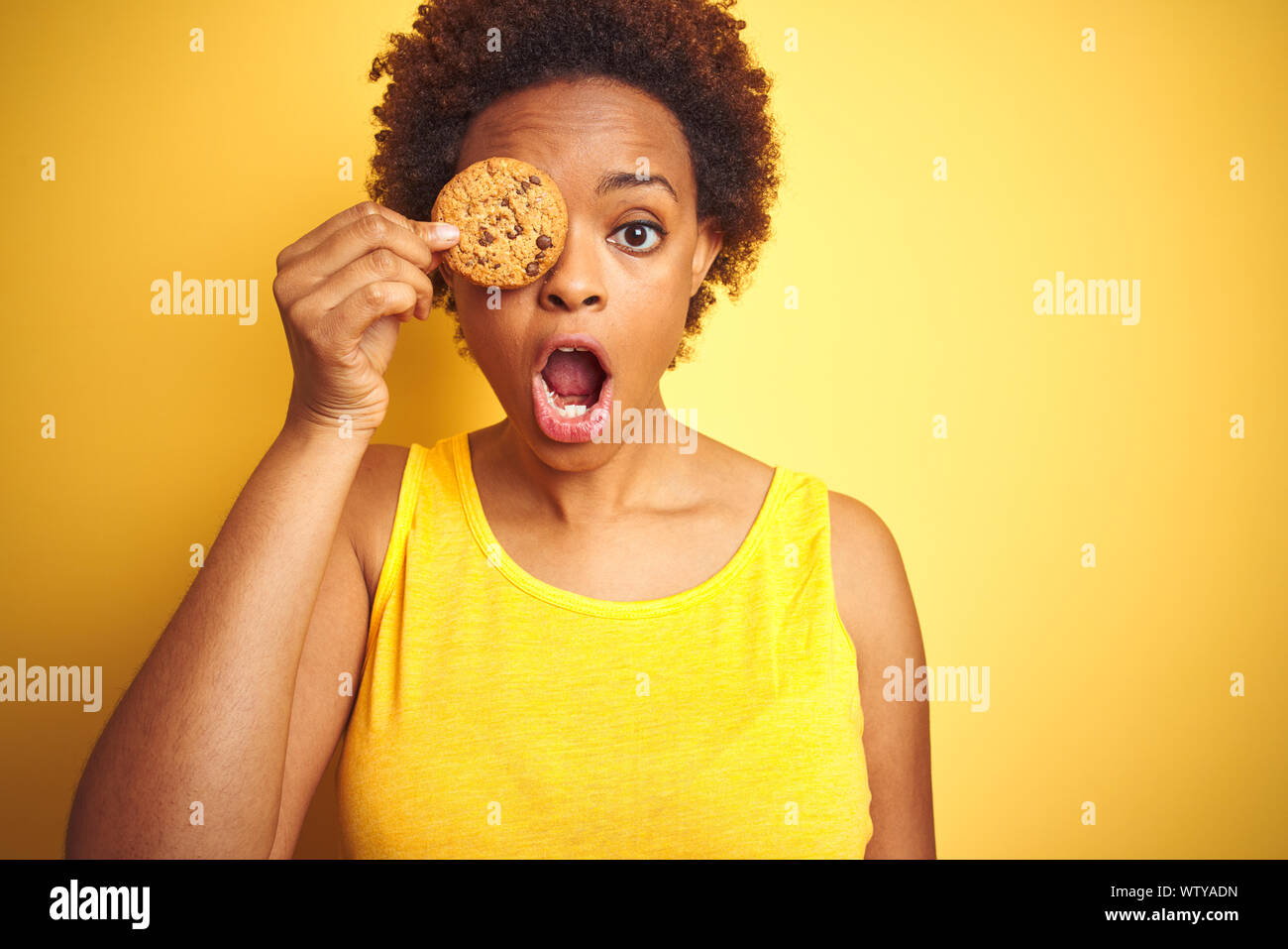 African american woman holding chocolate chips cookie over yellow ...