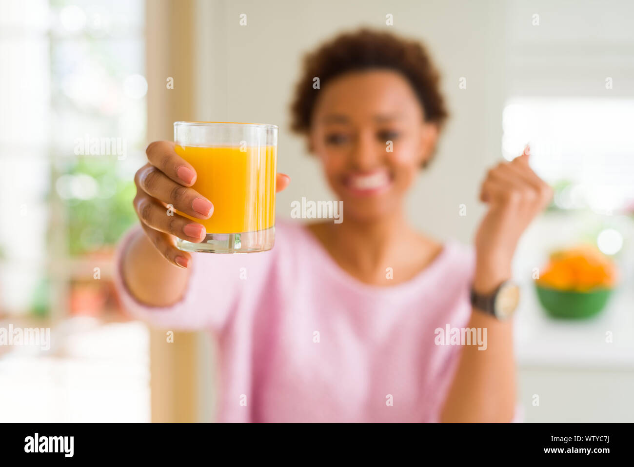 Young african american woman driking orange juice at home screaming ...