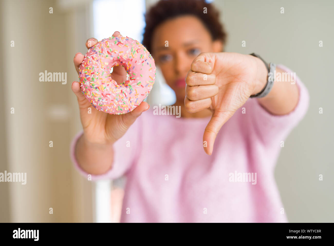 Young african american woman eating pink sugar donut with angry face ...