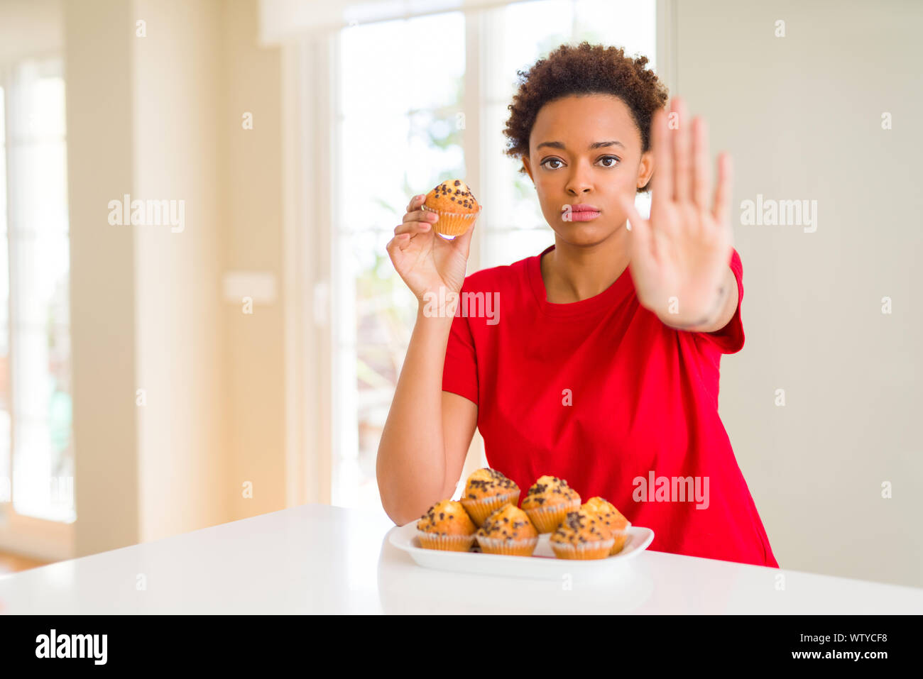 Young african american woman eating chocolate chips muffins with open ...