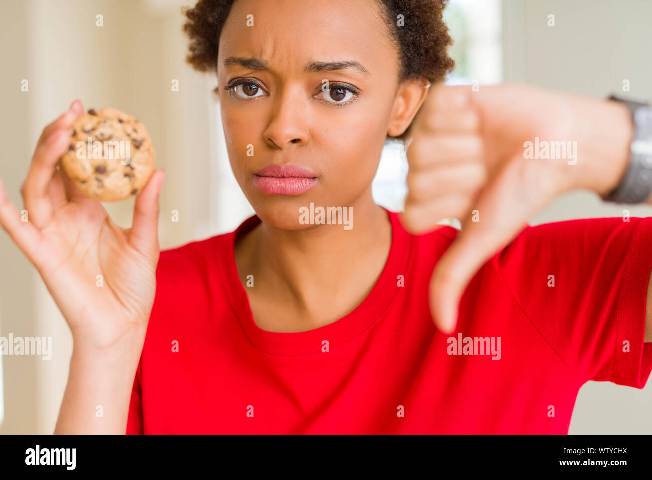 Young african american woman eating chocolate chips cookies with angry ...