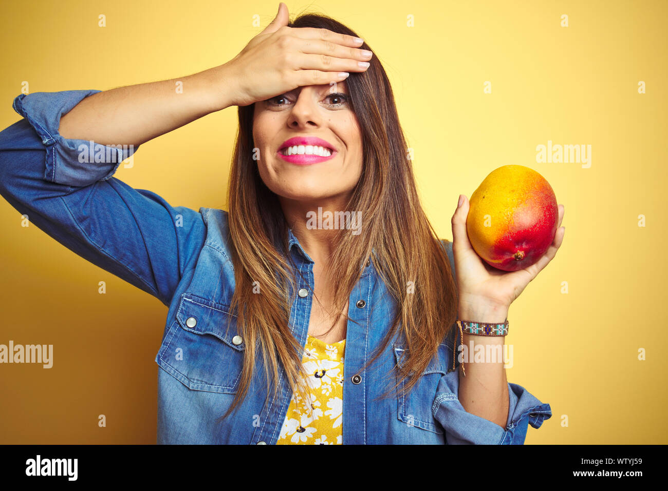 Young beautiful woman eating fresh healthy mango over yellow background ...