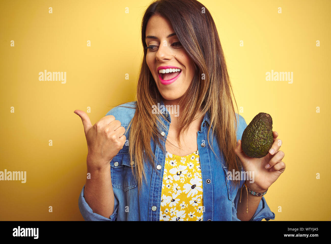 Young beautiful woman eating healthy avocado over yellow background ...