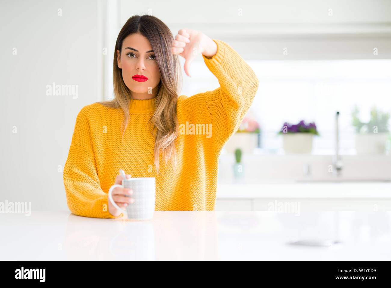 Young beautiful woman drinking a cup of coffee at home with angry face ...