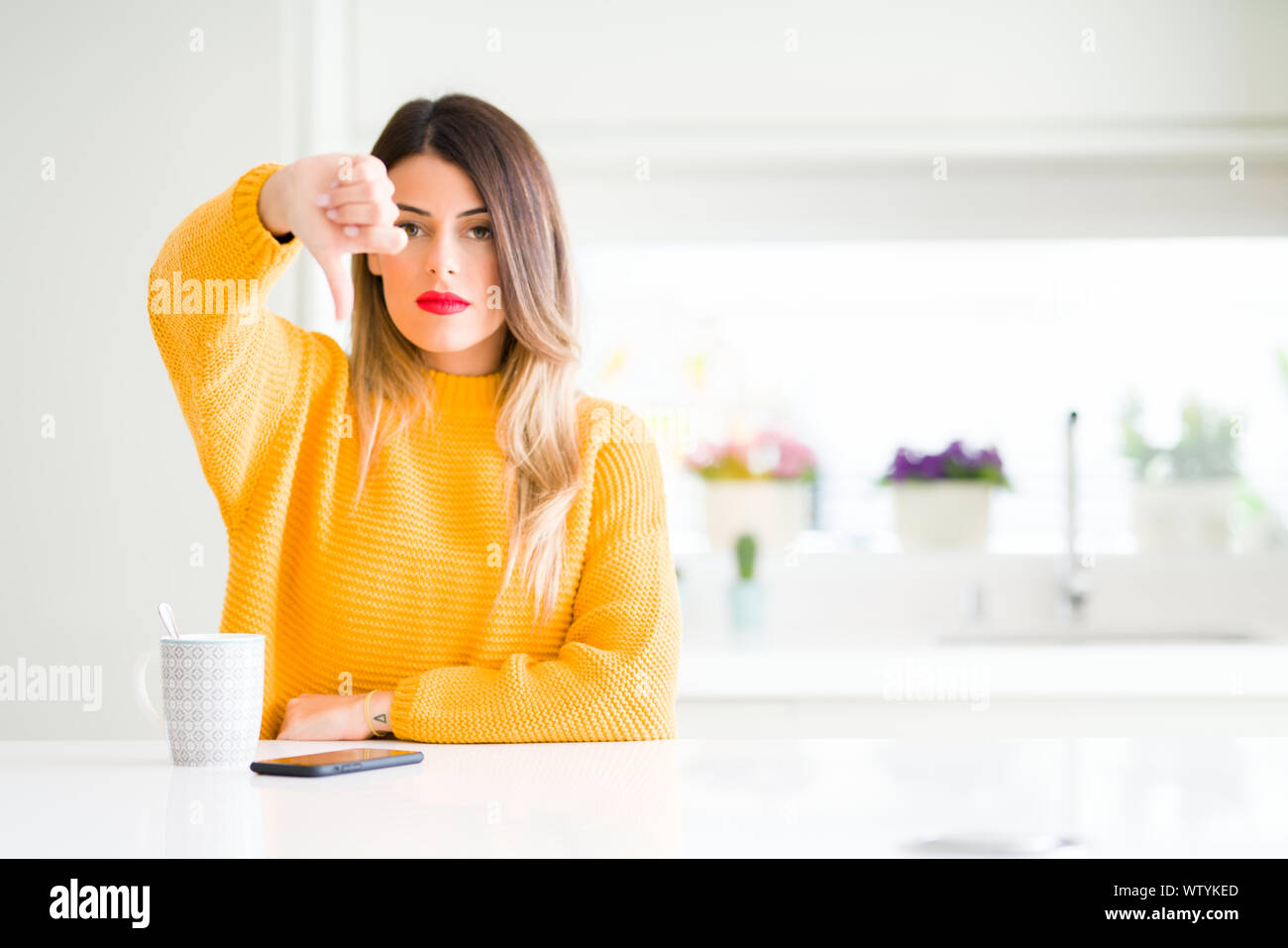 Young beautiful woman drinking a cup of coffee at home looking unhappy ...