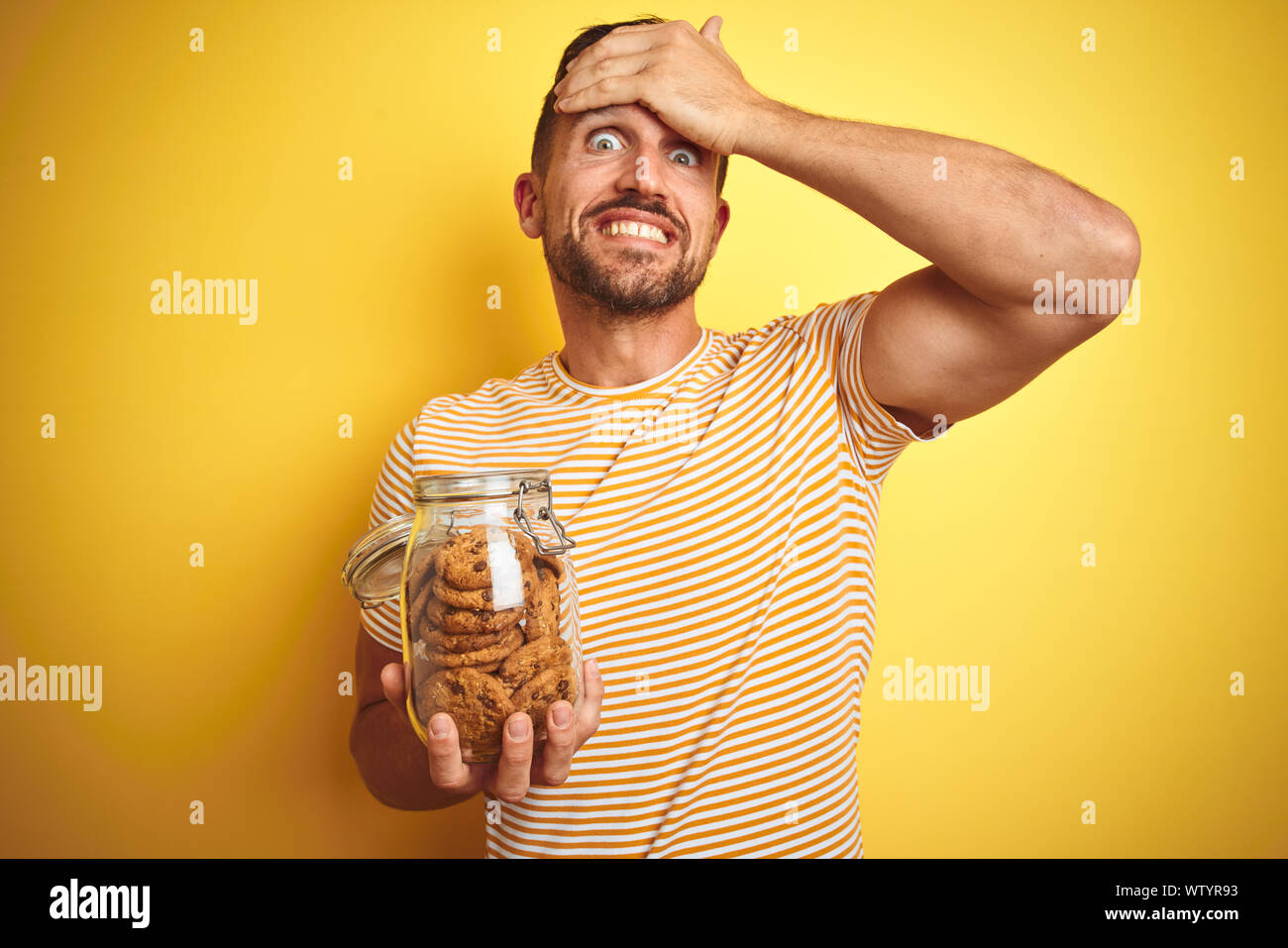 Young handsome man holding a jar of cookies over yellow isolated ...