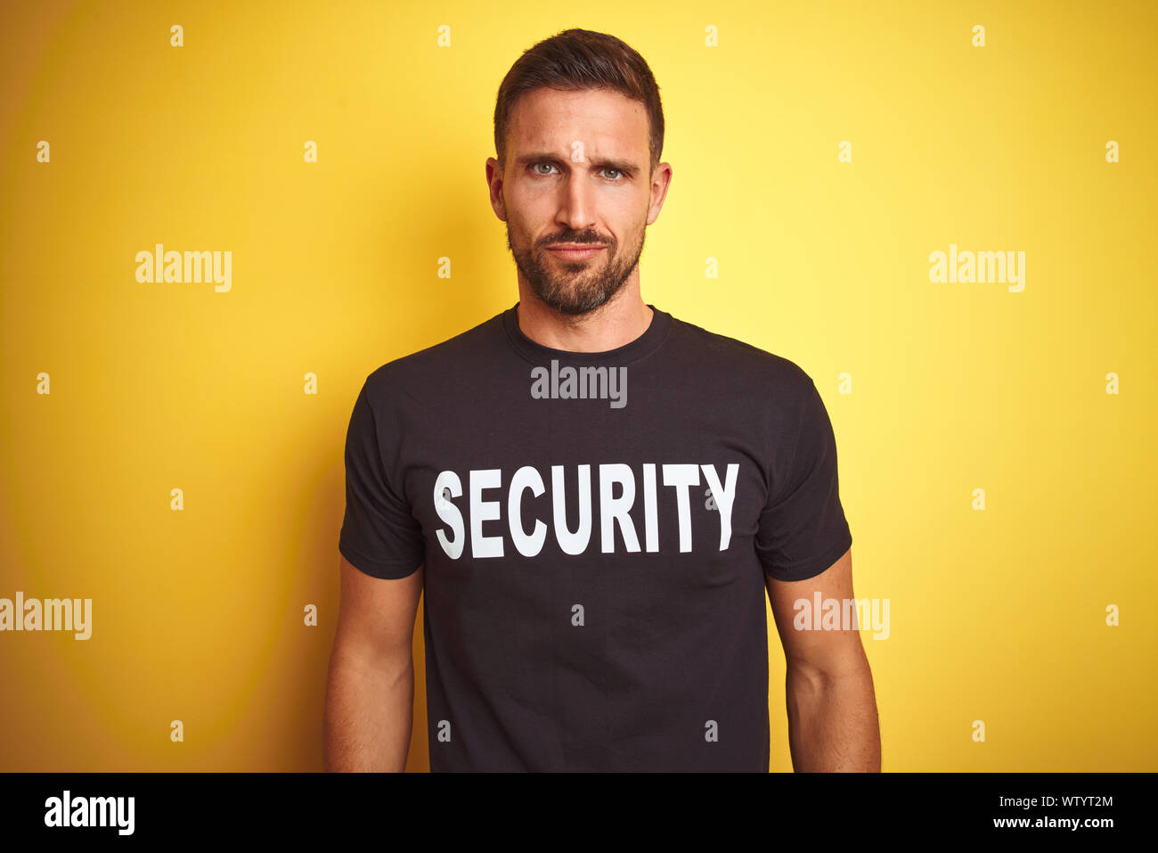 Young safeguard man wearing security uniform over yellow isolated ...