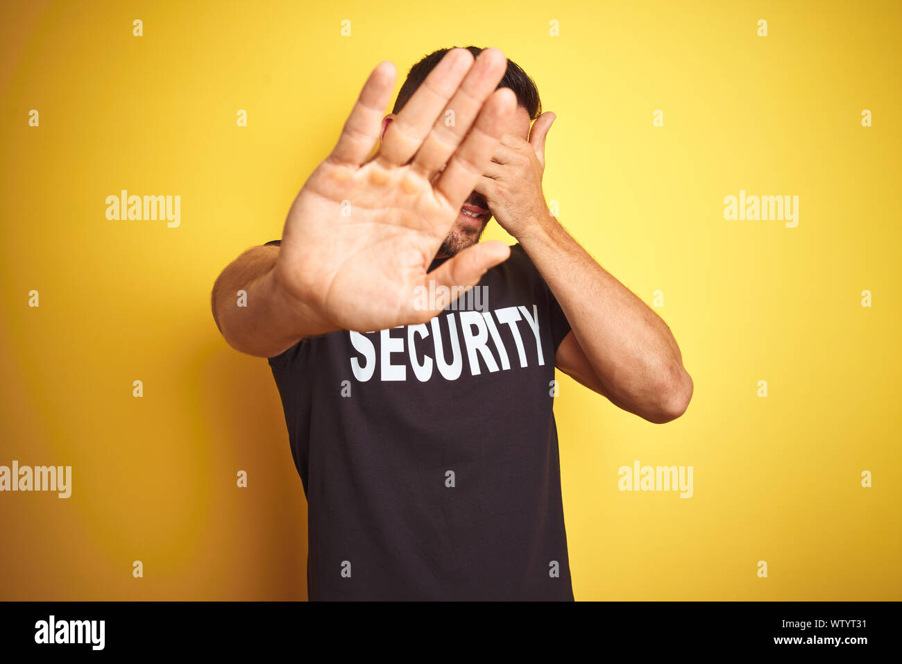 Young safeguard man wearing security uniform over yellow isolated ...