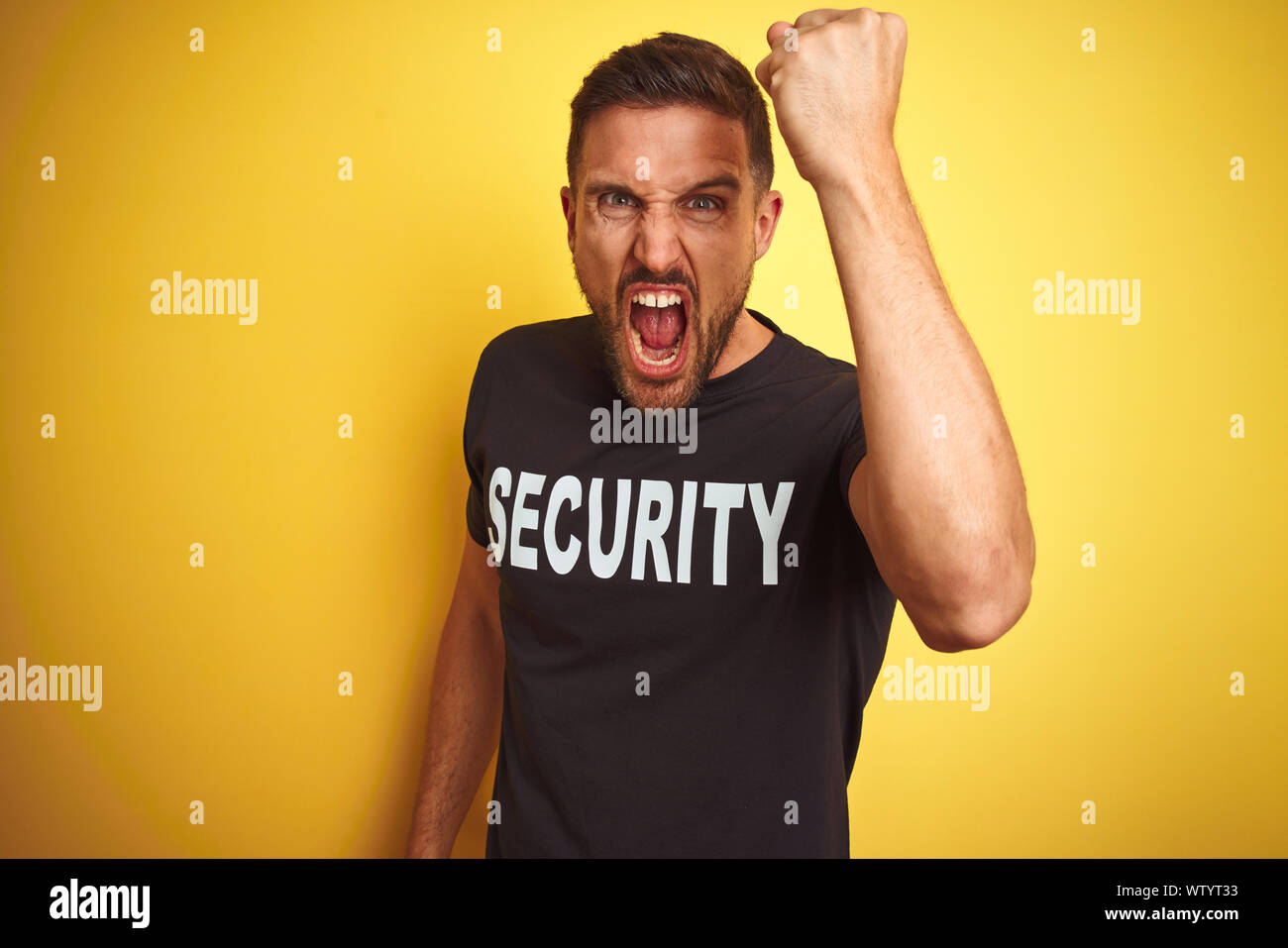Young safeguard man wearing security uniform over yellow isolated ...