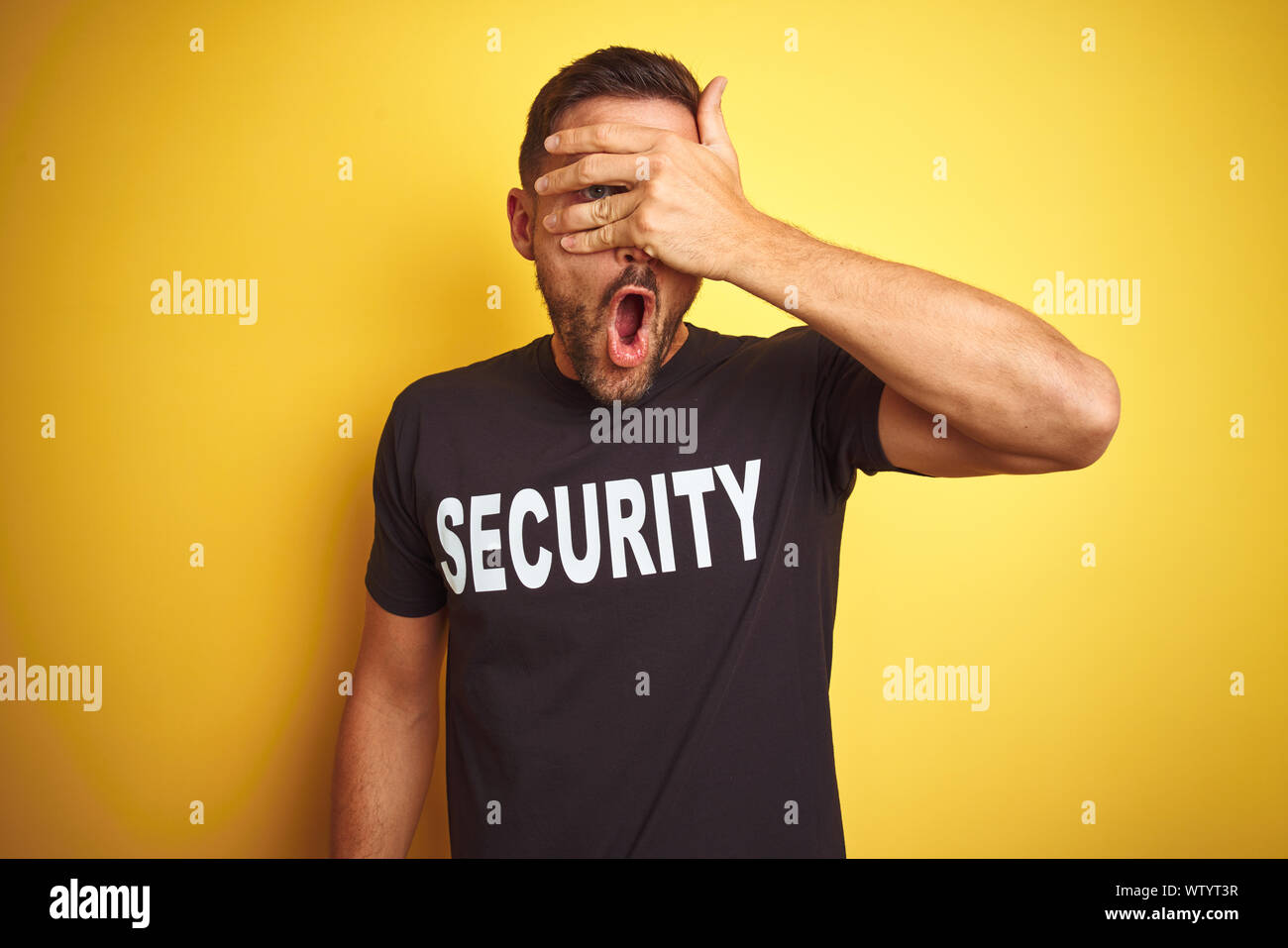 Young safeguard man wearing security uniform over yellow isolated ...