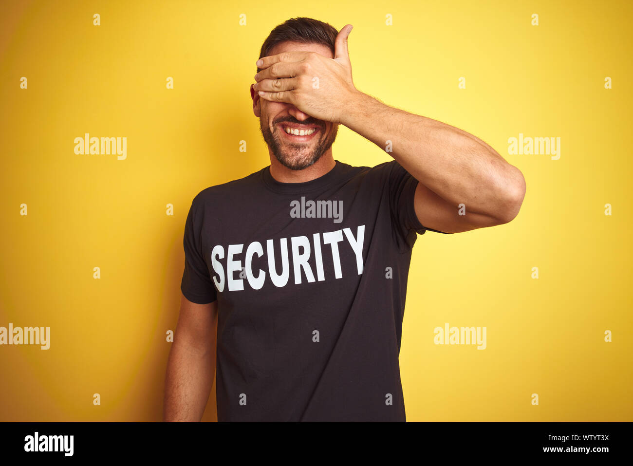 Young safeguard man wearing security uniform over yellow isolated ...