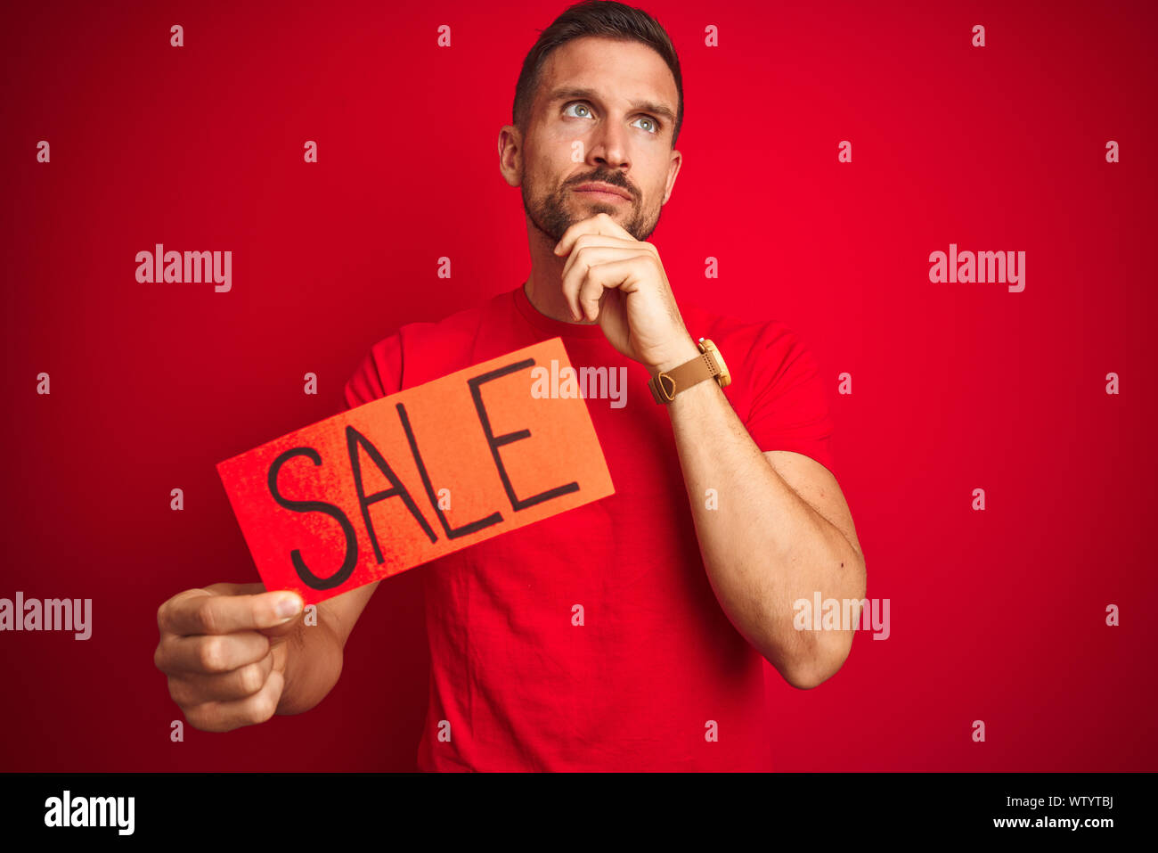 Young man holding sale advertising poster board over red isolated ...