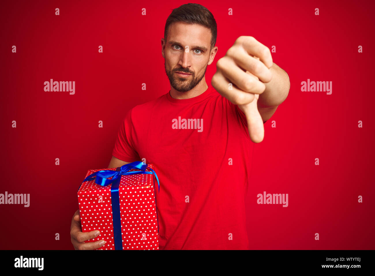 Young man holding birthday present over isolated red background with ...