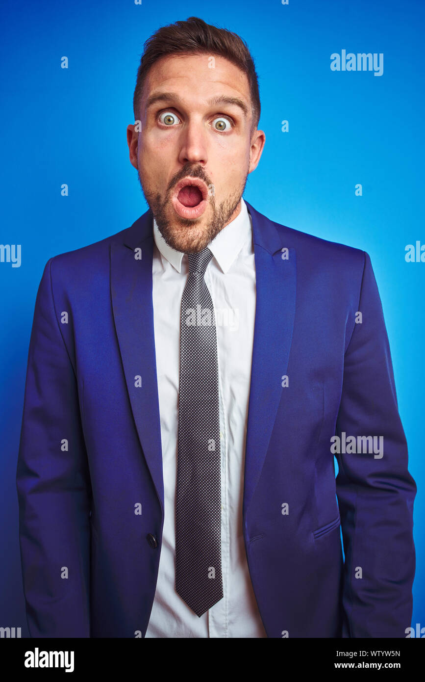 Vertical angle picture of young handsome business man over blue isolated background afraid and ...