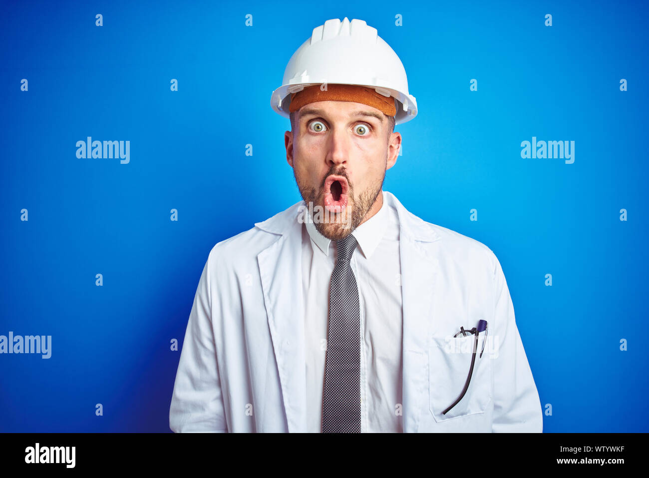 Young handsome engineer man wearing safety helmet over blue isolated ...